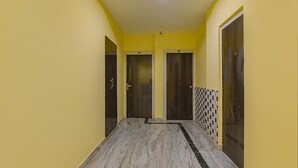 Corredor com paredes amarelas, duas portas e chão de azulejos.