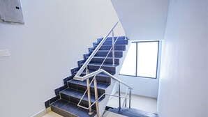 Uma escada moderna com corrimãos de metal, que leva a um quarto claro e arejado com uma grande janela.