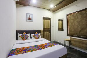 Quarto de hotel com cama, cabeceira de madeira, quadro na parede e uma janela grande com cortina estampada.