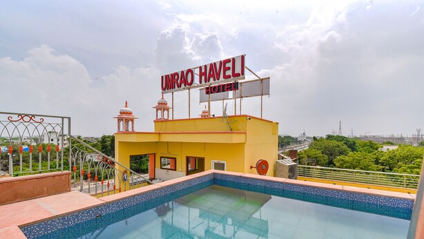 Um hotel com piscina, uma placa com a inscrição 'UMRAO HAVELI HOTEL' e vista para o horizonte da cidade ao fundo.