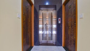 Um elevador moderno com soalho de mármore e portas de madeira, com painel digital e botões de emergência.