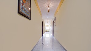 Um corredor comprido e estreito com piso de mármore, obras de arte nas paredes e um lustre.