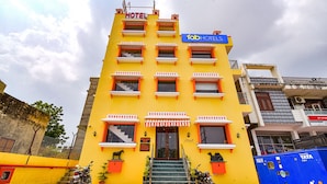 Um hotel com vários andares e fachada amarela vibrante, com uma escadaria que leva à entrada e uma placa indicando ser um hotel.
