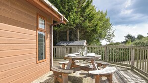 Um deck de madeira com mesas de piquenique e uma porta de vidro que dá para uma cabana.