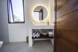 Casa de banho com espelho redondo, porta de madeira e prateleira com cestos.