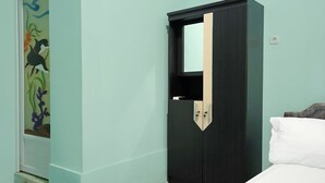 Quarto com paredes verde-água, guarda-roupa preto com espelho e cama com roupa de cama branca.