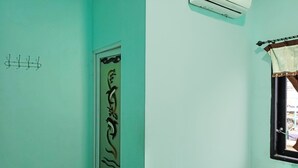 Quarto com paredes verde-água, porta de madeira com detalhe decorativo, um pequeno banquinho de madeira e uma janela com cortina.