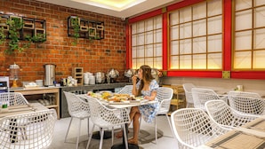 Restaurante com paredes de tijolo, cadeiras brancas e janela emoldurada em vermelho.