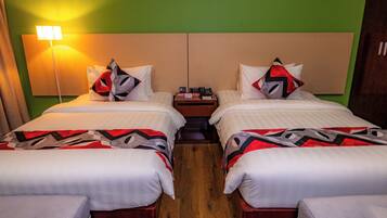 Quarto de hotel com duas camas, uma mesinha de cabeceira com telefone e uma luminária.
