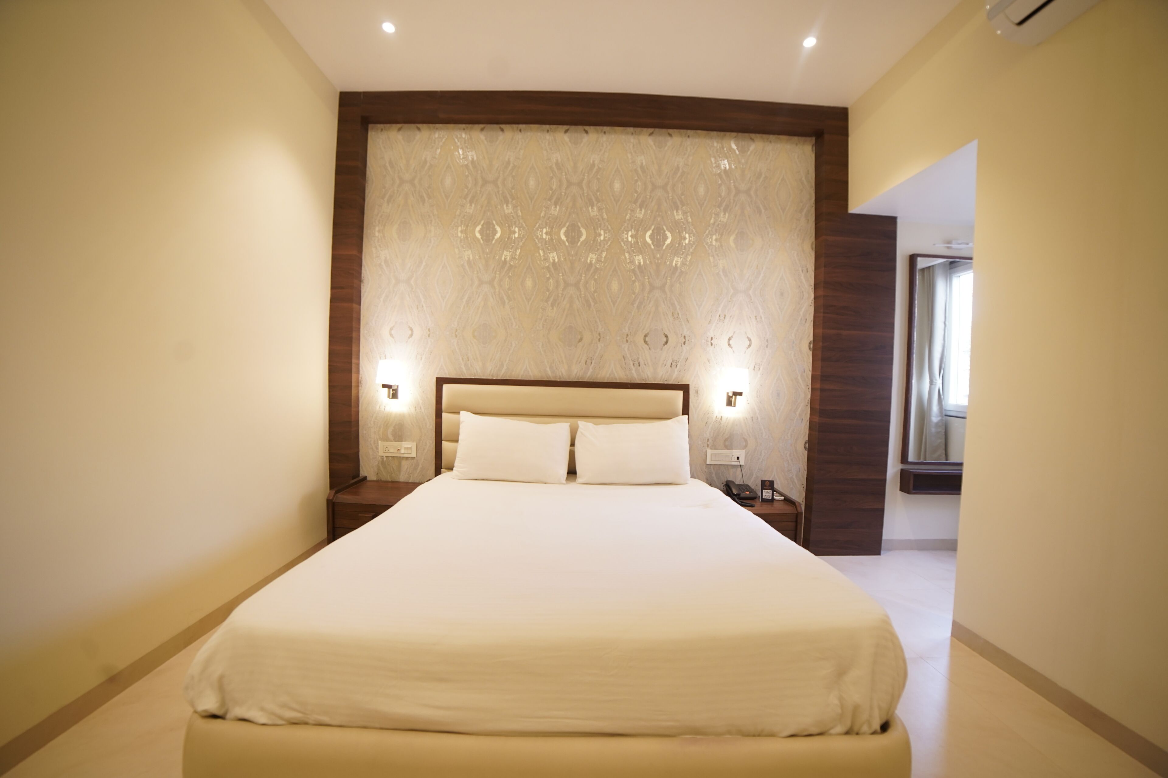 Uma cama grande com cabeceira de madeira, duas mesas de cabeceira com luminárias, e uma parede estampada atrás da cama.