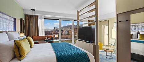 Quarto de hotel com cama, televisão, secretária e vista para a paisagem urbana.