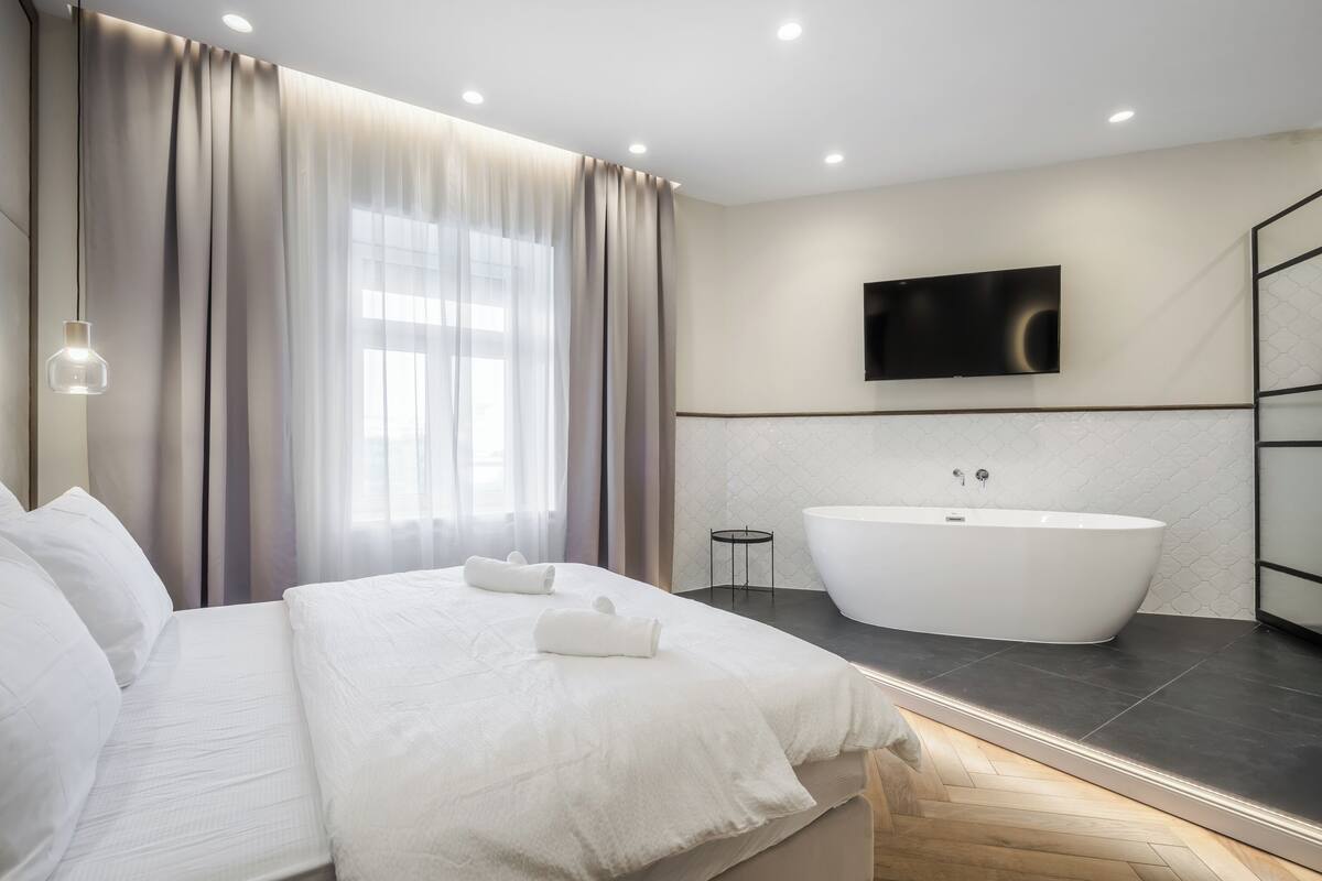 Quarto de hotel moderno com uma cama grande, uma banheira e uma TV de tela plana.