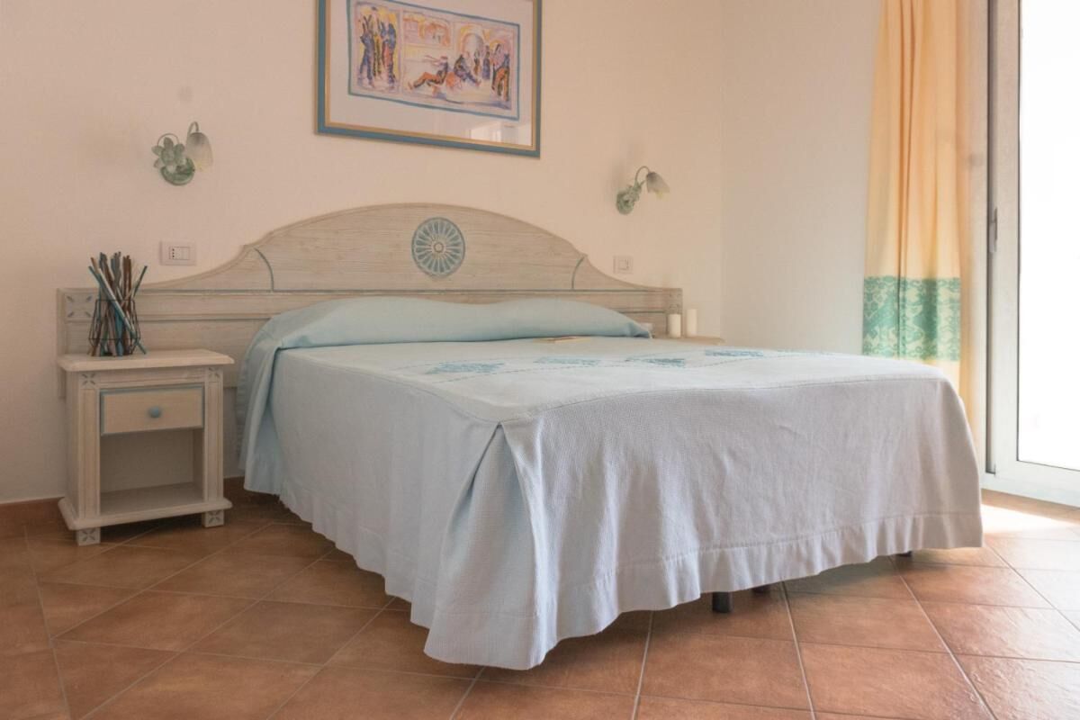 Quarto com cama, mesa de cabeceira, arandelas e um quadro.