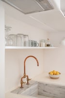 Cozinha com bancada de mármore, torneira de cobre e um recipiente com limões.