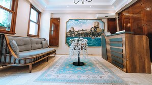 Quarto com sofá de madeira, um arranjo floral, pintura de uma paisagem costeira e um balcão de recepção.
