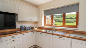 Cozinha moderna com armários brancos, bancada de madeira e janela com vista para o verde.