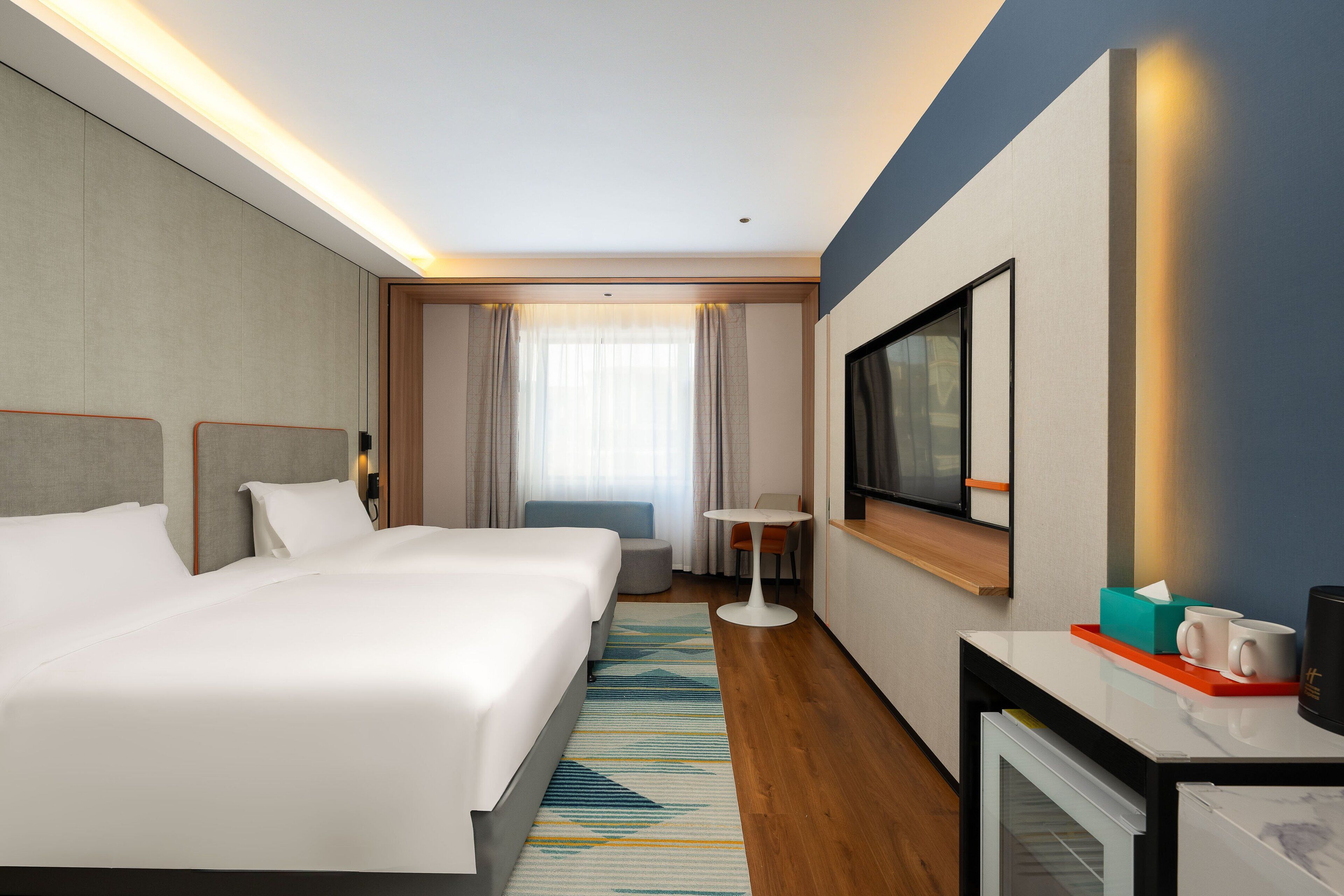 Quarto de hotel com cama, mesa de cabeceira, televisão e vista para o exterior pela janela.