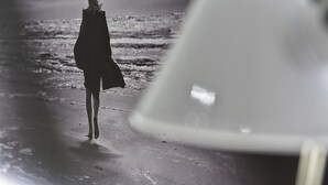 Uma pessoa caminhando na praia com um objeto desfocado em primeiro plano.