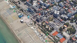 Vista aérea de uma cidade costeira com praia, edifícios e pontos de interesse marcados.