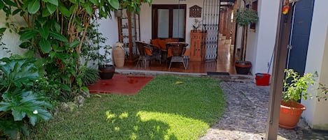 Um pátio com caminho de pedra, um pequeno gramado e área de estar com móveis de vime.