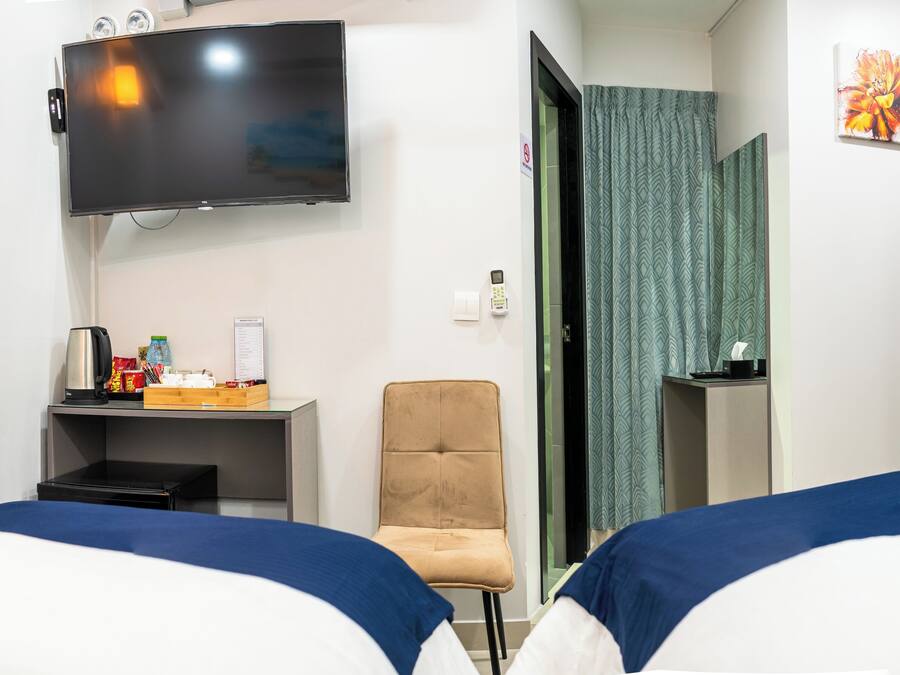 Quarto de hotel com duas camas, televisão, escrivaninha com cadeira, mesinha e porta do banheiro.