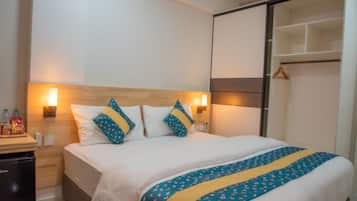 Cama bem arrumada com manta de padrão floral, cabeceira de madeira e luminárias laterais.