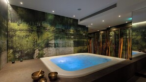 Um spa moderno com uma grande banheira de hidromassagem, um espaço de meditação em madeira e um mural temático de floresta.
