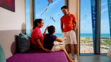 Uma família de três pessoas num quarto com uma grande janela com vista para a praia.