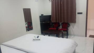 Quarto de hotel com cama, escrivaninha, cadeira, televisão e espelho.