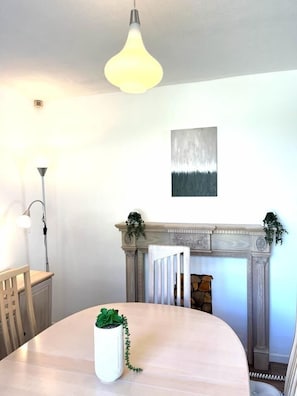 Uma área de refeições com uma mesa redonda, cadeiras, um lustre, uma lareira com parapeito e uma obra de arte emoldurada na parede.