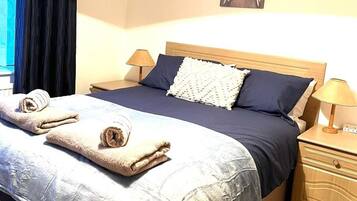 Uma cama bem arrumada com cabeceira azul, duas luminárias de mesa e uma obra de arte na parede.