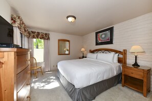 Um quarto com cama, mesas de cabeceira de madeira, cômoda, cadeira, espelho e janela com cortinas.