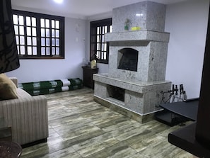 Sala de estar com lareira de pedra, sofá, mesa de centro e janela com persianas.