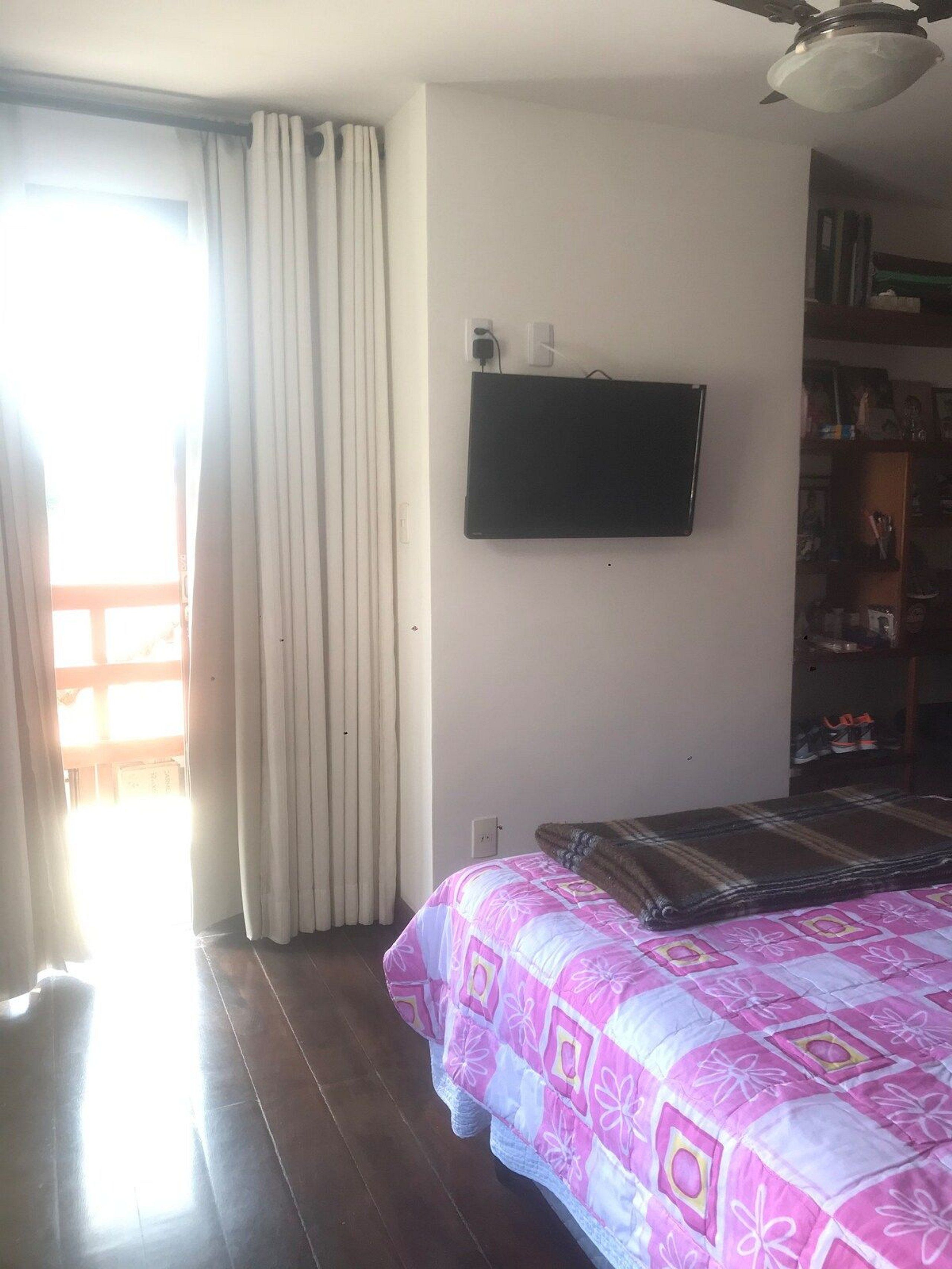 Quarto com uma cama, televisão na parede e uma estante de livros.