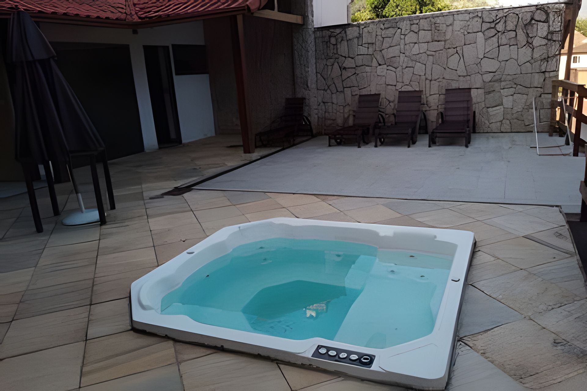 Uma banheira de hidromassagem em um quintal com uma parede de pedra e móveis de exterior.