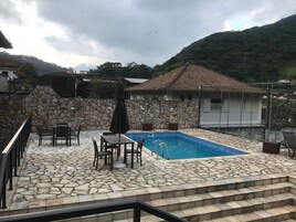 Área externa com piso de pedra, piscina, parede de pedra e vista para uma paisagem montanhosa.