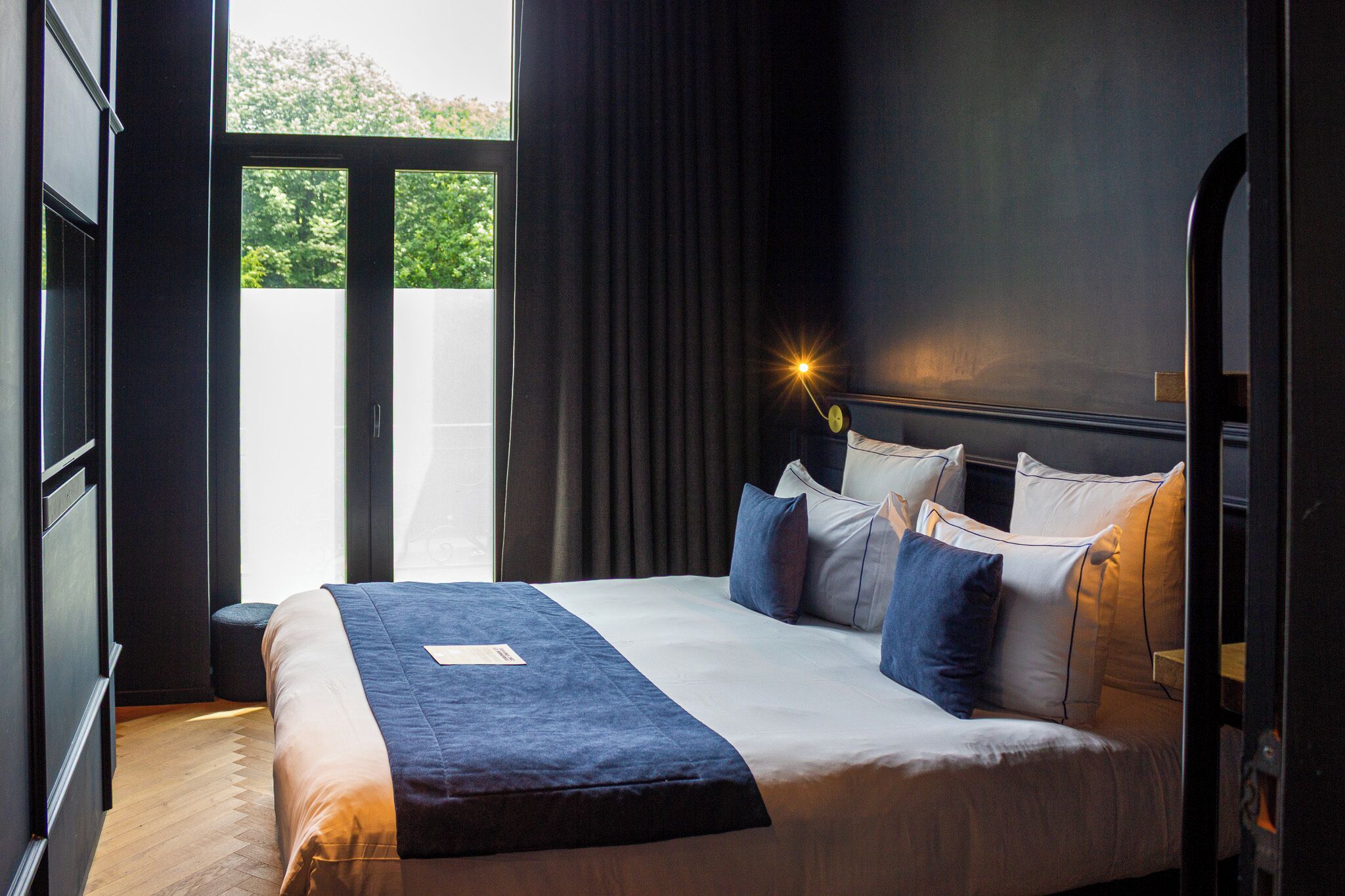 Quarto de hotel moderno com uma cama grande, uma mesa de cabeceira e vista para o exterior.
