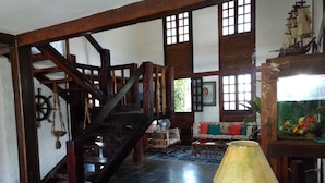 Um quarto espaçoso com escada de madeira, uma mesa redonda com abajur, um sofá e um modelo de navio.