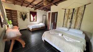 Quarto com teto de madeira, duas camas, uma mesinha com uma planta e uma janela com cortinas.