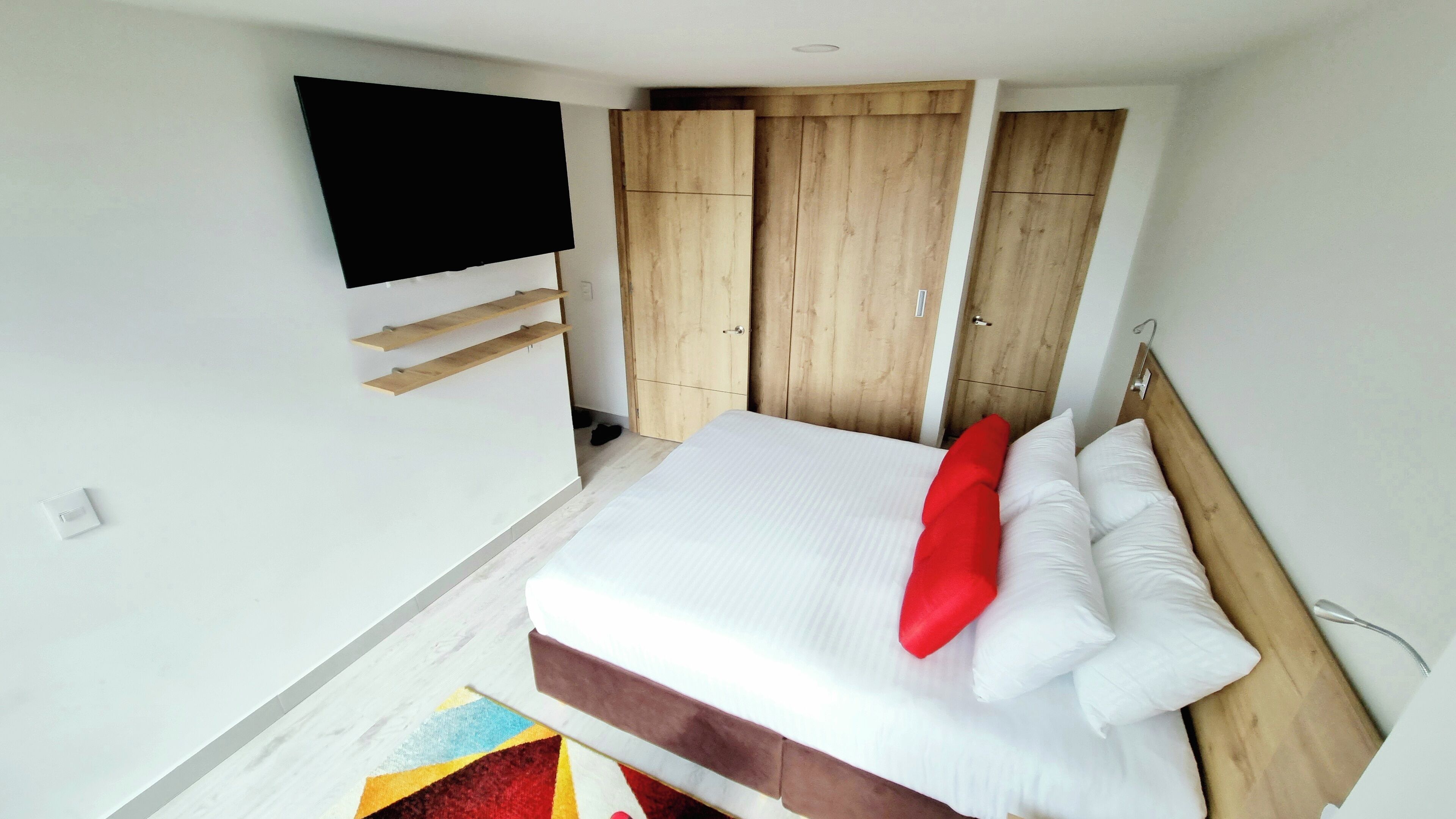 Quarto com cama, televisão fixada na parede e guarda-roupa com portas deslizantes.