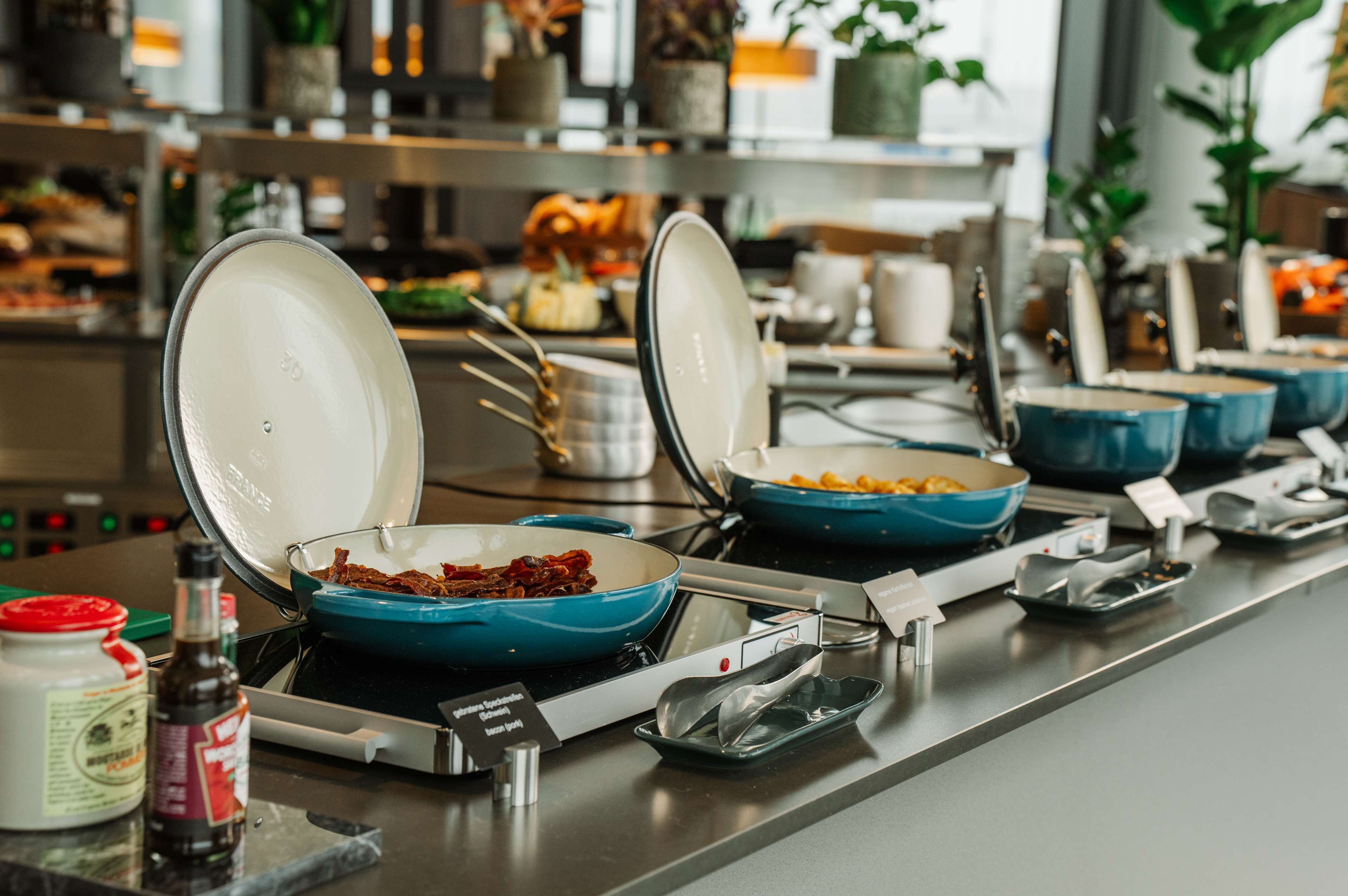 Disposição de buffet com recipientes azuis contendo alimentos, uma garrafa de molho e uma placa indicando o tipo de comida.