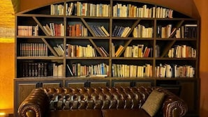 Um sofá de couro com encosto alto e estante embutida repleta de livros.