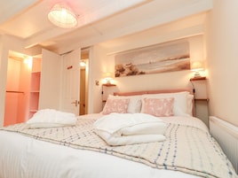 Cama bem arrumada com travesseiros e toalhas dobradas, um quadro na parede e um abajur em uma mesa de cabeceira.