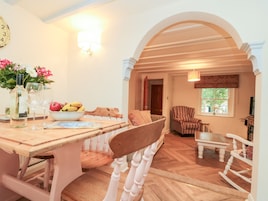 Uma área de refeições com mesa de madeira, cadeiras brancas e um arranjo floral.