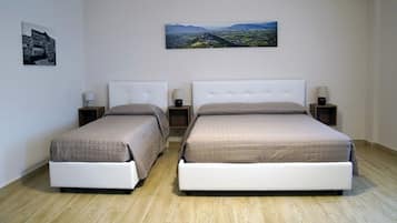 Quarto duplo com duas camas, cada uma com cabeceira branca e colcha bege acolchoada. Há duas mesas de cabeceira com abajures, e um quadro de paisagem pendurado acima das camas.