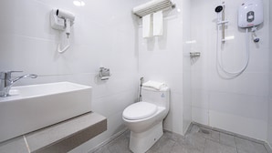 Uma casa de banho moderna com uma sanita, chuveiro e lavatório brancos.