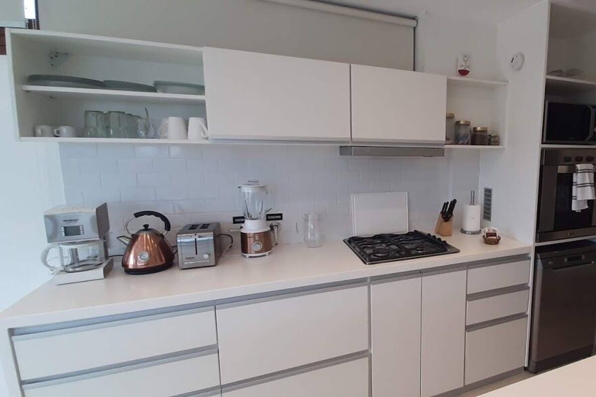 Uma cozinha moderna com armários brancos, fogão a gás, micro-ondas, chaleira e máquina de lavar.