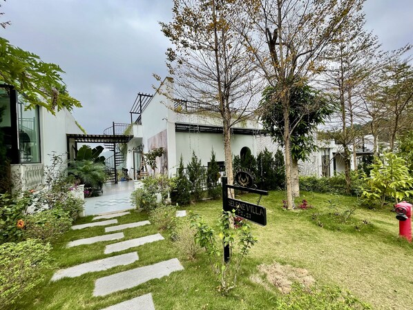 Uma villa moderna com um caminho de pedra que leva à entrada, rodeada por vegetação exuberante e um jardim bem cuidado.