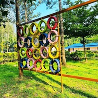 Estrutura colorida de pneus em área externa gramada, com árvores e um edifício ao fundo.