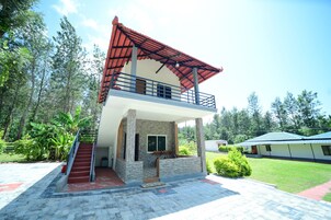 Um edifício de dois andares com telhado vermelho, varanda e escadaria que leva à entrada.